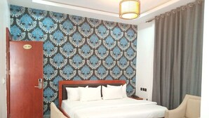 Quarto de hotel com cama, duas cadeiras, uma mesinha e uma porta.
