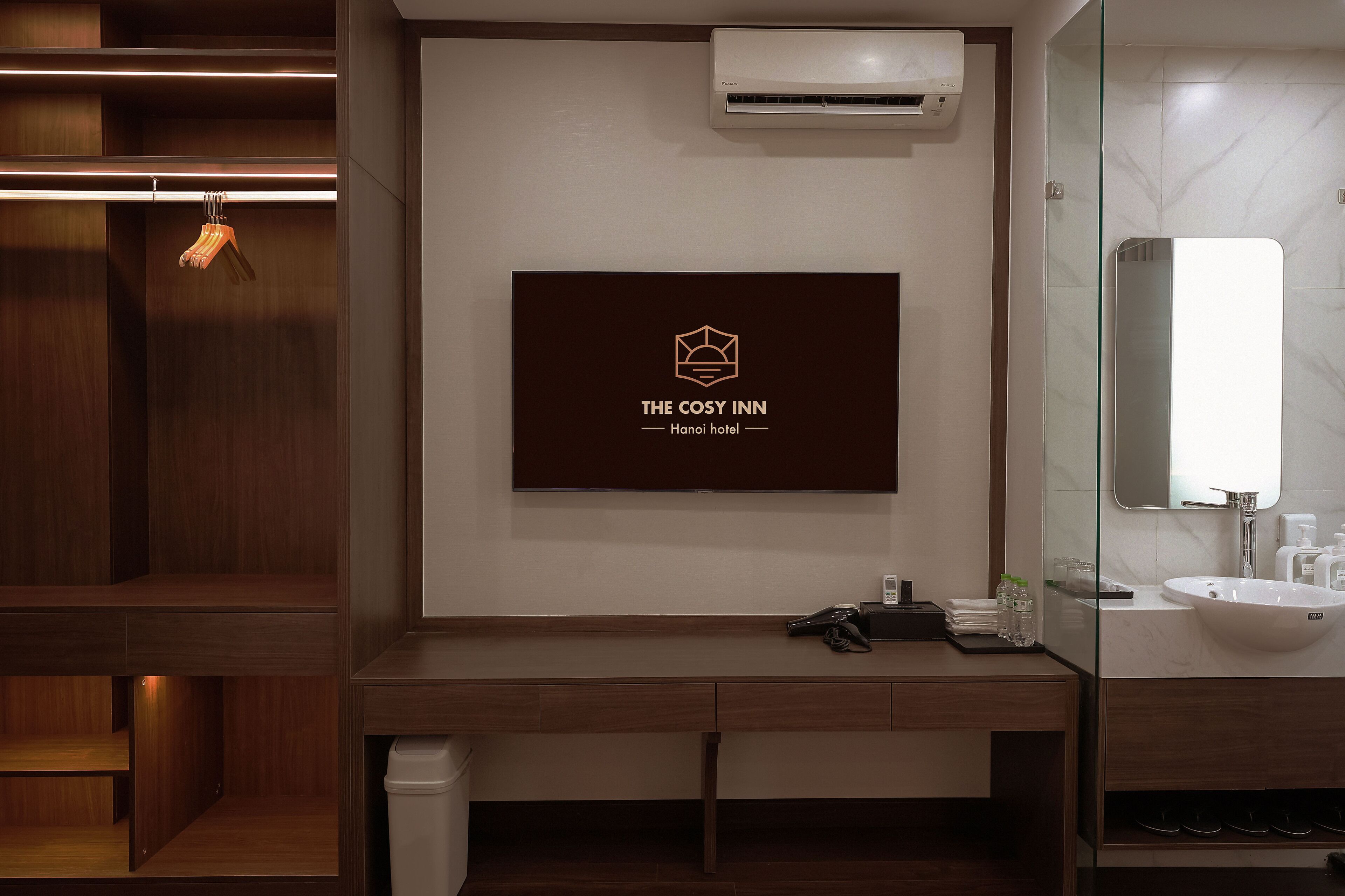 Um banheiro de hotel com toucador, espelho, pia e um aviso emoldurado acima do espelho.