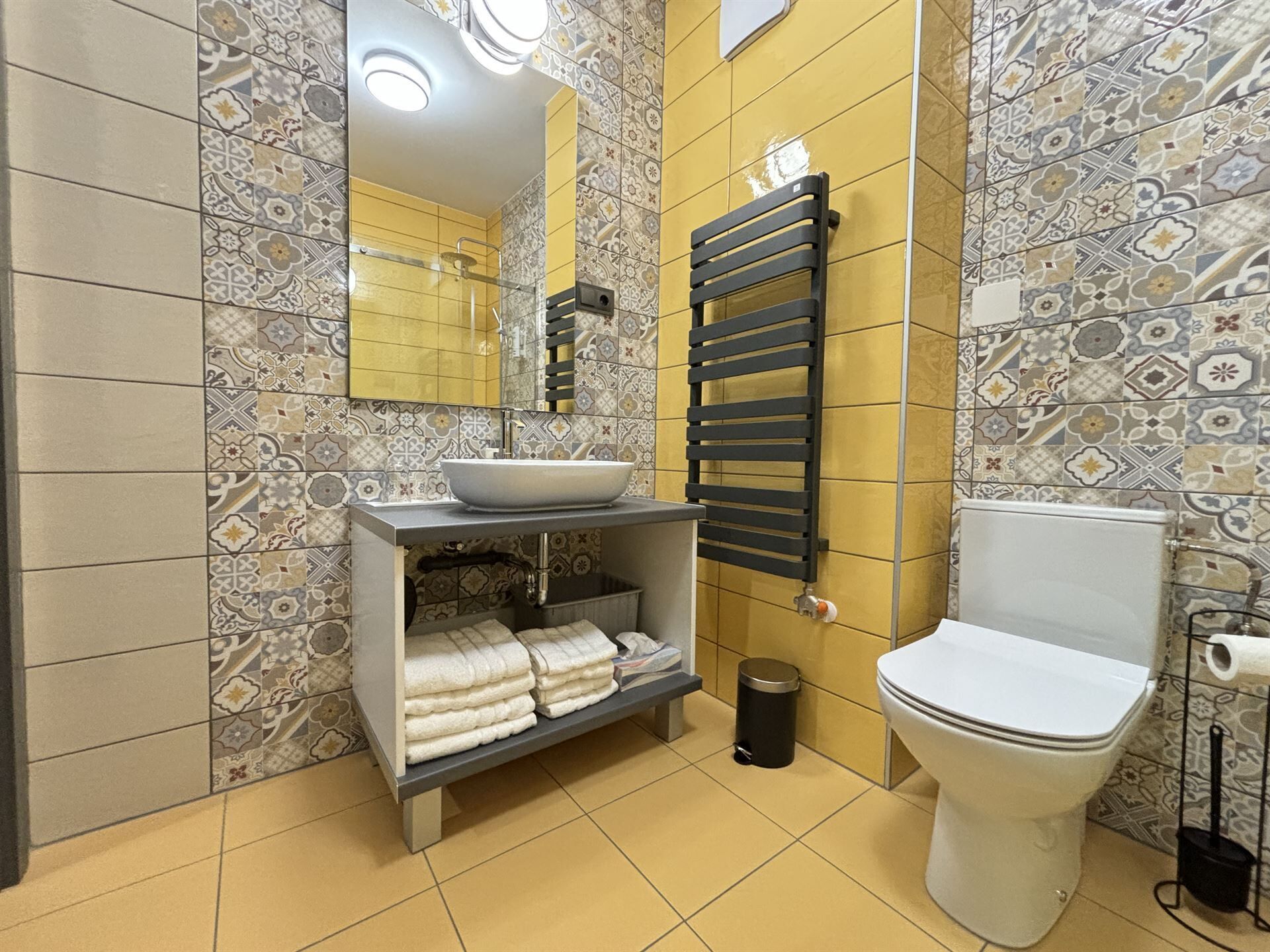 Um banheiro com vaso sanitário branco, pia suspensa, porta-toalhas e azulejos estampados.