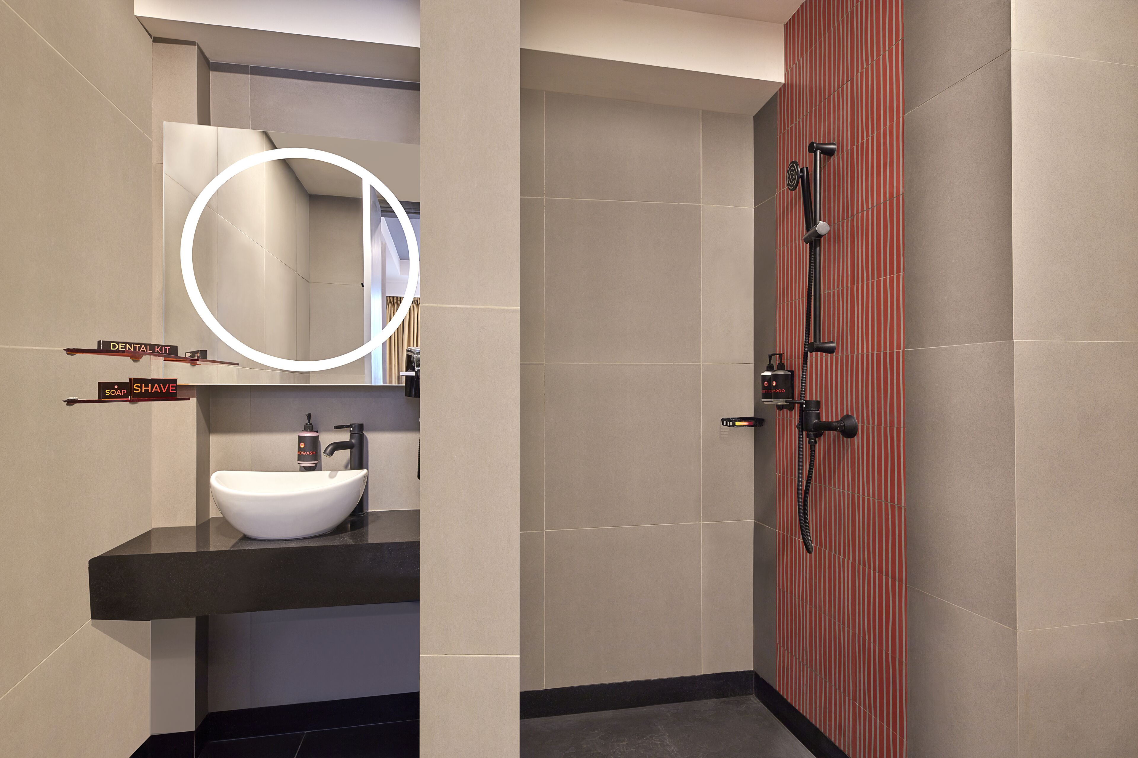 Uma casa de banho moderna com uma pia branca, um espelho com luz circular e uma área de duche com parede listrada em vermelho.