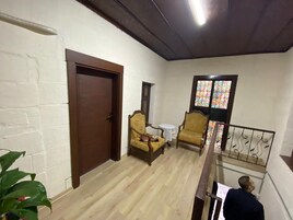 Um quarto com porta de madeira, uma mesa pequena, duas cadeiras e uma janela com vitrais.