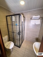 Casa de banho com chuveiro em cabine de vidro, sanita e lavatório.