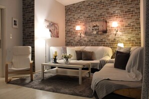 Uma sala de estar aconchegante com parede de tijolos, um sofá branco, uma poltrona branca e uma mesa de centro com velas e flores.