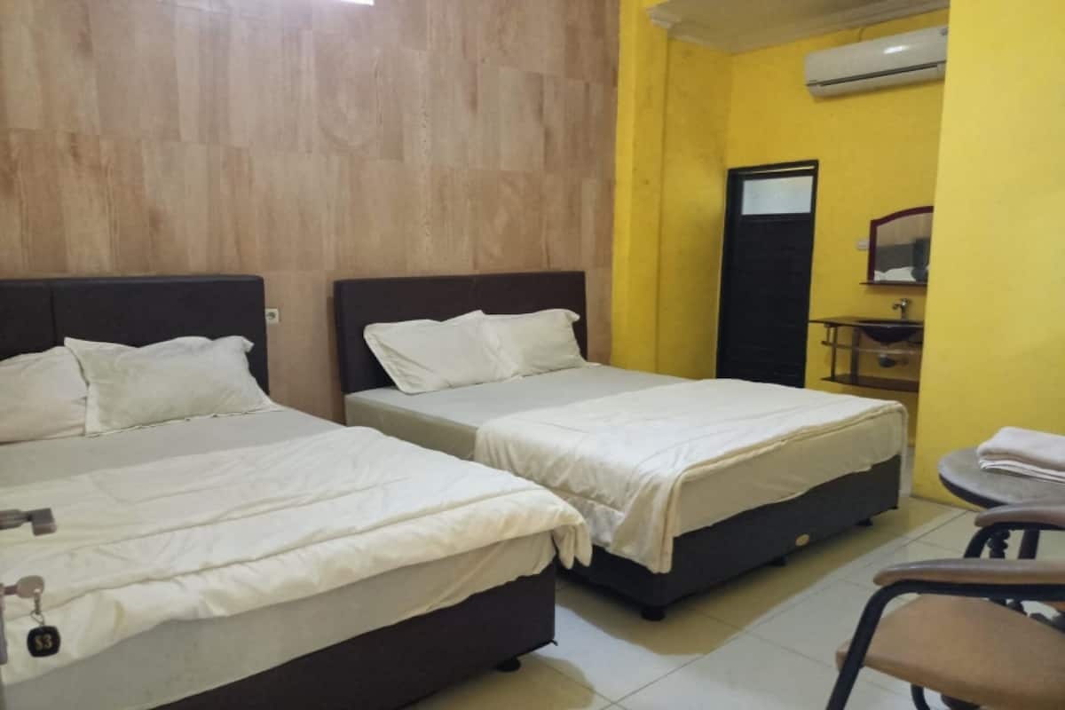 Quarto de hotel com duas camas, uma mesinha, uma cadeira, uma pia e um espelho.
