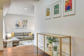 Uma sala de estar moderna com um sofá modular, uma mesa de centro de vidro e um aparador com plantas. Há obras de arte emolduradas na parede.