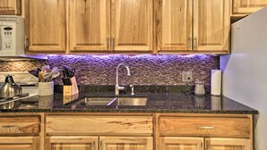 Cozinha com armários de madeira, bancada de granito, pia de aço inoxidável e backsplash iluminado em roxo.