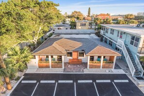 Um edifício de dois andares com telhado plano, um alpendre coberto e um estacionamento com vagas demarcadas.