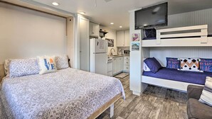 Quarto compacto com cama, sofá-cama, televisão e cozinha compacta.