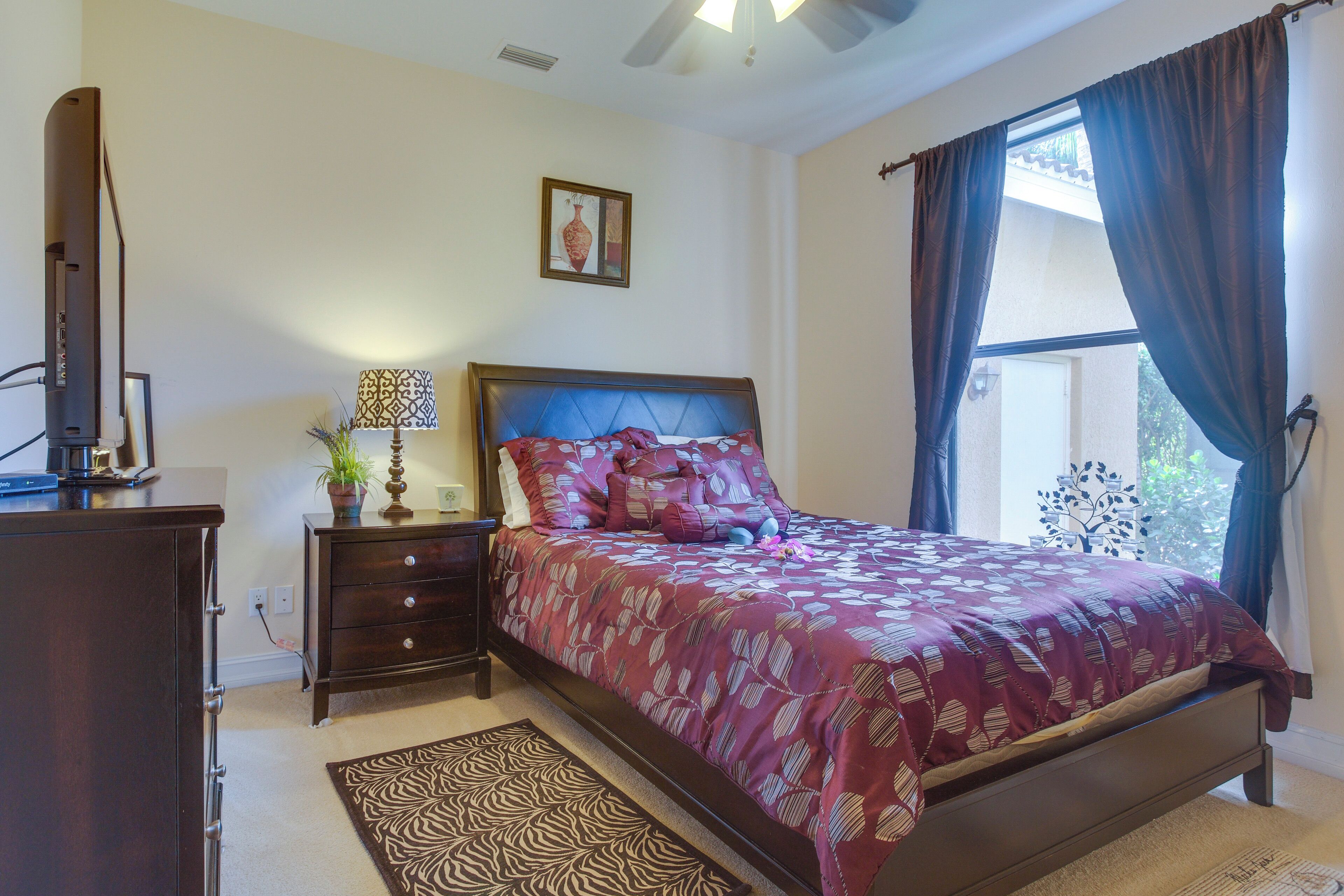 Quarto com cama, mesa de cabeceira, abajur, cômoda e janela com cortinas.