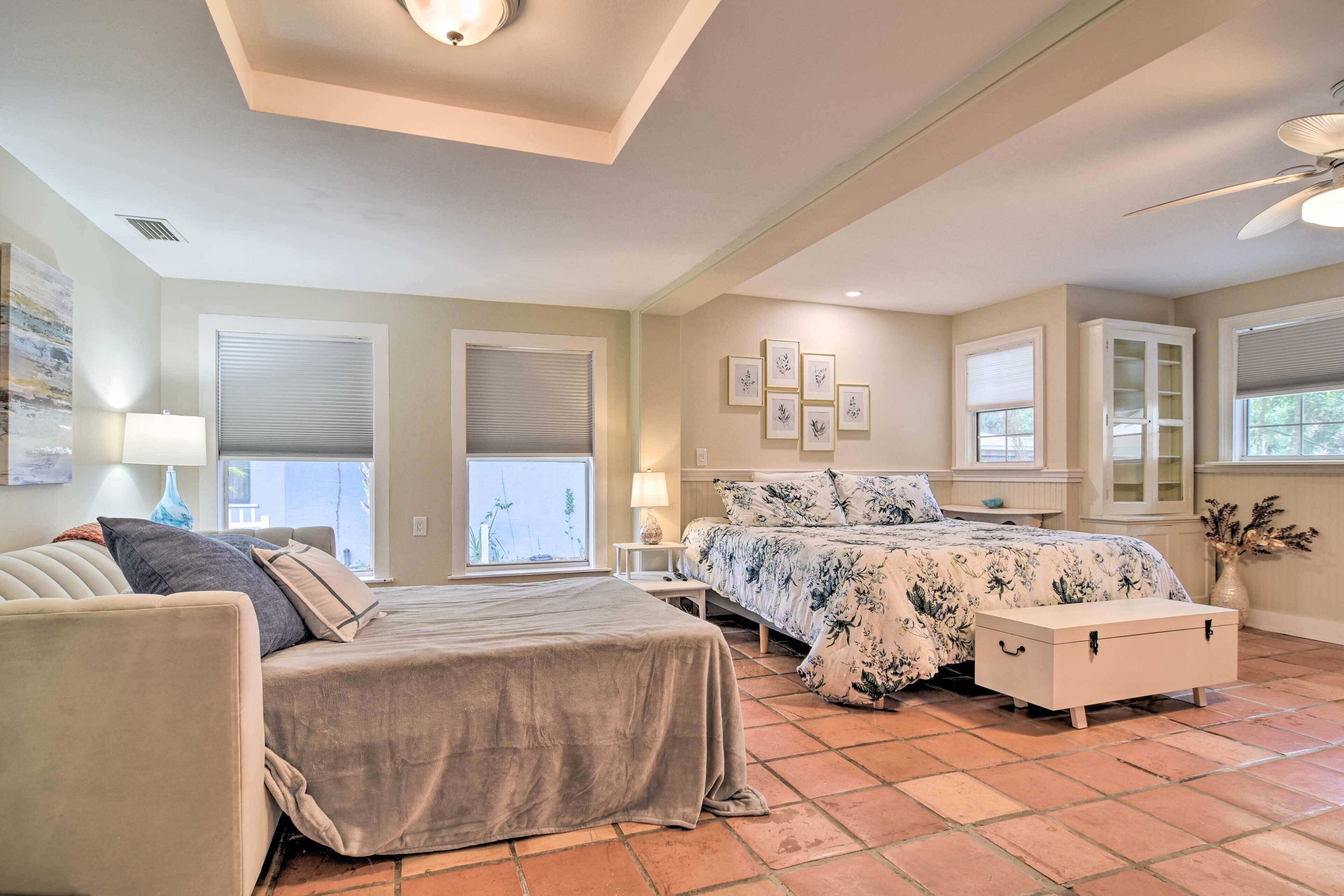 Quarto com cama, sofá, mesa de cabeceira, cômoda e janela com persianas.
