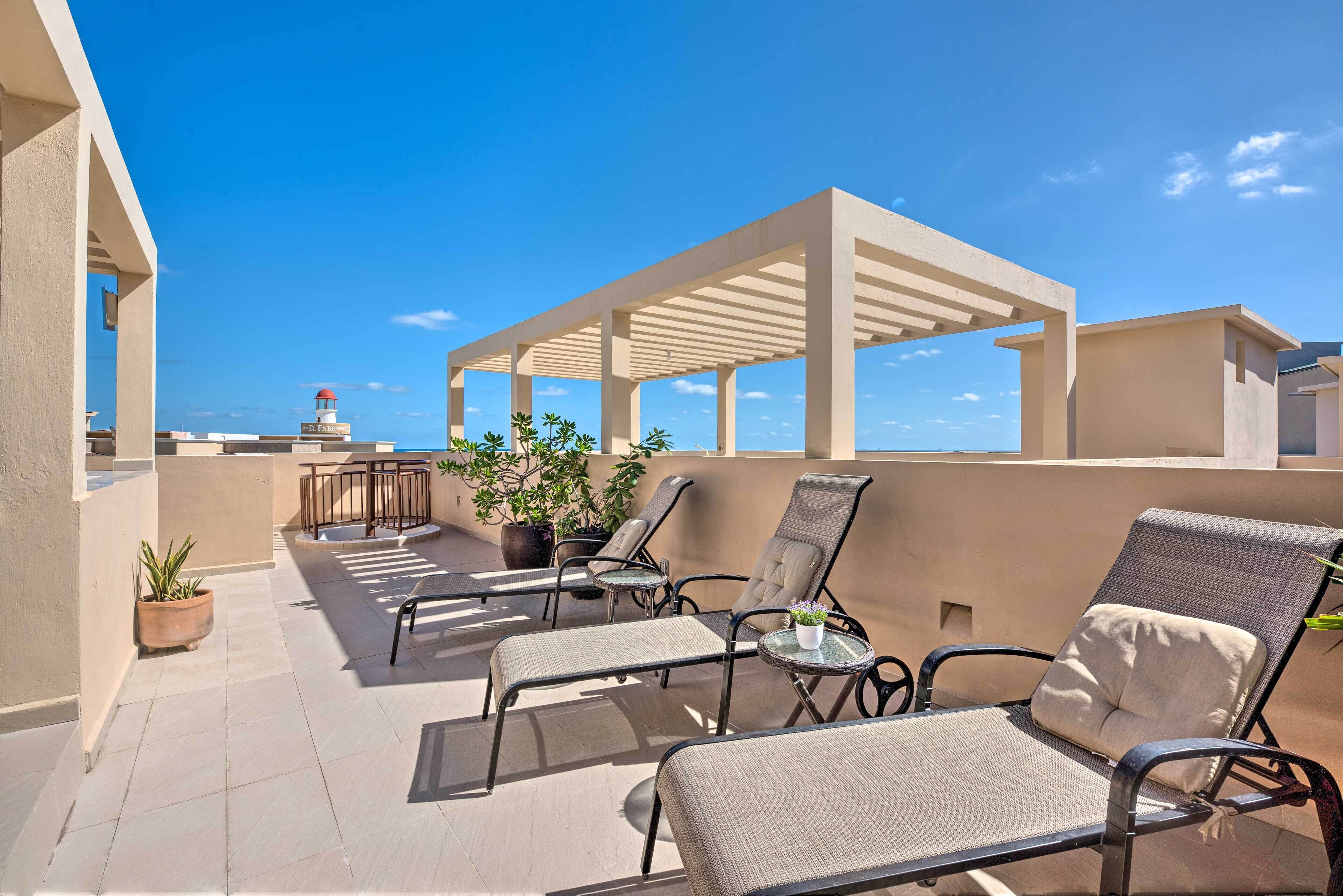 Terraço no telhado com cadeiras de lounge, um pérgola e vista para um farol.