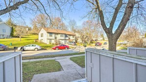 Uma rua residencial com casas, um carro vermelho estacionado na rua e uma árvore em primeiro plano.