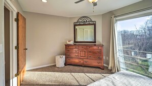 Quarto com uma janela grande, ventoinha no teto, cómoda e chão coberto de carpete.