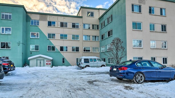 Um edifício residencial com vários andares e uma área de estacionamento na frente.