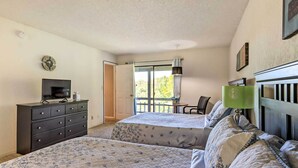 Quarto com duas camas, penteadeira, televisão e varanda com mesa e cadeiras.