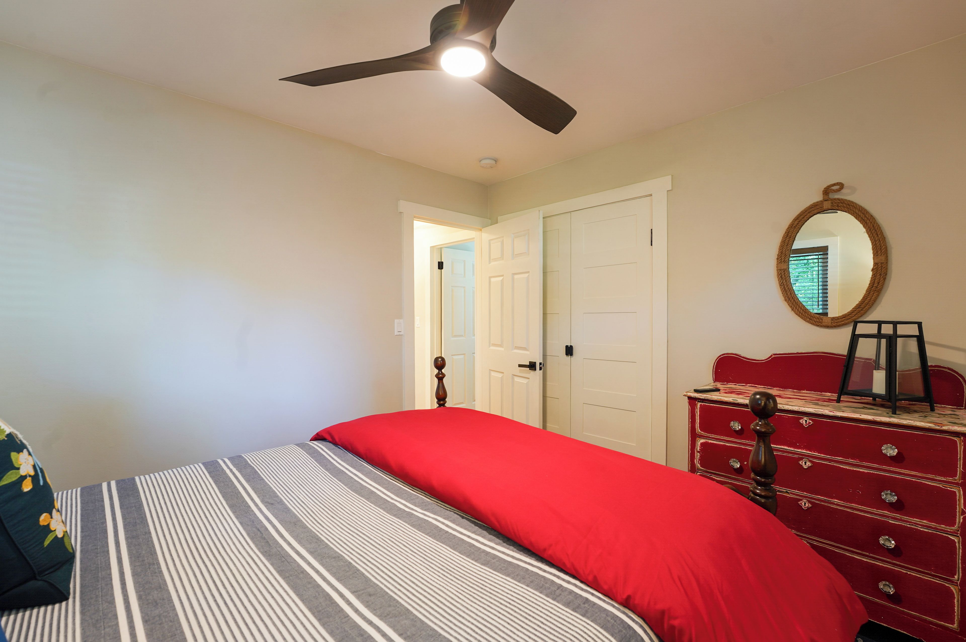 Quarto com cama, cômoda, espelho e ventilador de teto.