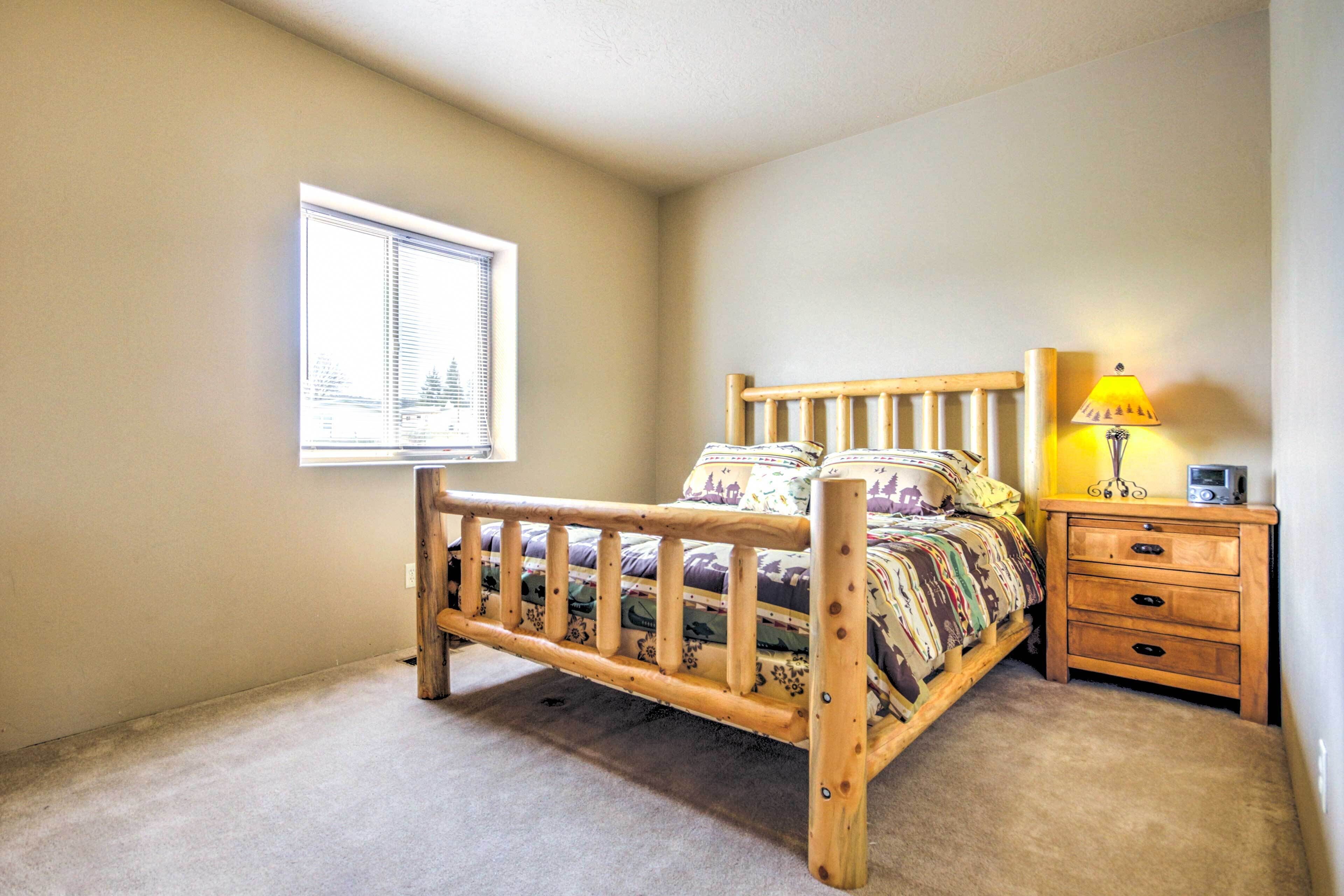 Quarto com cama de madeira, mesa de cabeceira com gavetas, abajur e janela com persianas.