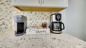 Cozinha com cafeteira, máquina Keurig e uma caixa com a etiqueta 'coloque um pouco de açúcar'.