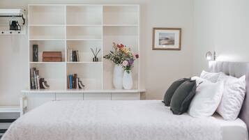 Um quarto com uma cama grande, um guarda-roupa branco e uma mesinha com um vaso de flores.