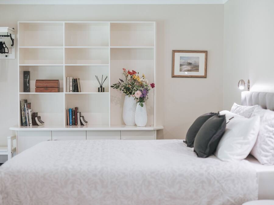 Um quarto com uma cama grande, um guarda-roupa branco e uma mesinha com um vaso de flores.