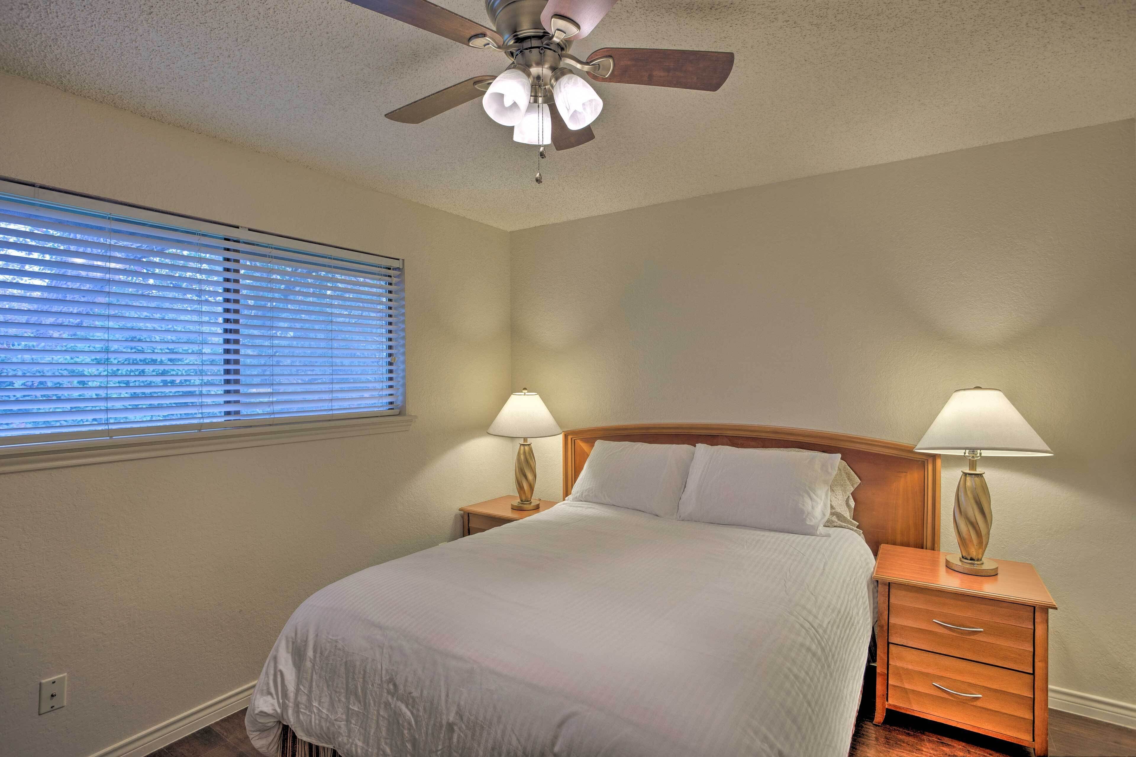 Quarto com cama, duas mesas de cabeceira com luminárias, um ventilador de teto e uma janela com persianas.