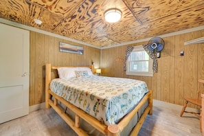 Quarto com painéis de madeira, uma cama, uma janela, um ventilador e uma porta.