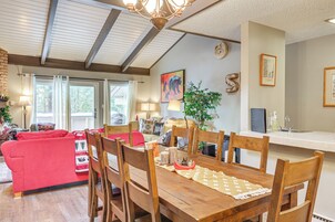 Uma sala de estar aconchegante com um sofá vermelho, mesa de jantar de madeira e cadeiras. Há uma janela com cortinas, uma planta e um quadro na parede.