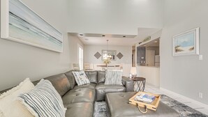 Uma sala de estar moderna com um sofá modular, uma mesa de centro e uma área de jantar ao fundo.