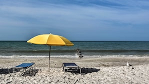 Uma praia com duas espreguiçadeiras e um guarda-sol amarelo.