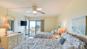 Quarto de hotel com duas camas, ventoinha no teto, televisão e varanda com vista para o mar.
