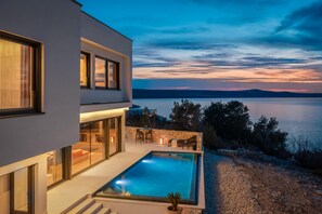 Uma casa moderna com piscina, área de estar externa e vista para um lago ao entardecer.