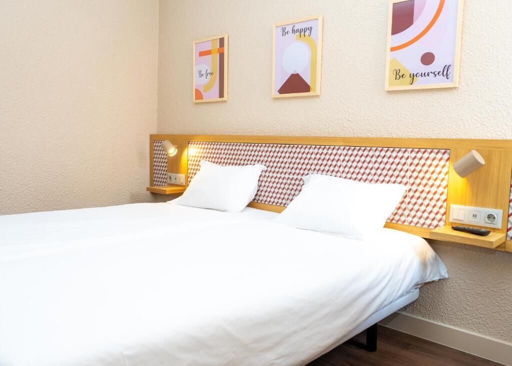 Cama bem arrumada com lençóis brancos, cabeceira estampada, abajures laterais e quadros de parede inspiradores.