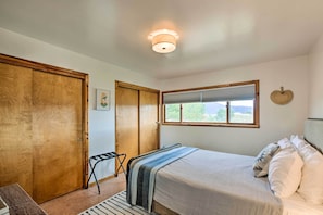 Quarto com cama, janela, porta e uma cadeira pequena.