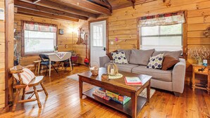 Interior acolhedor de uma cabana com piso de madeira, um sofá, uma mesa de centro, uma mesa de jantar com cadeiras e uma lareira.