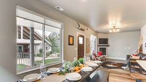 Uma ampla sala de jantar com uma mesa longa posta para refeição, grandes janelas e vista para o exterior.