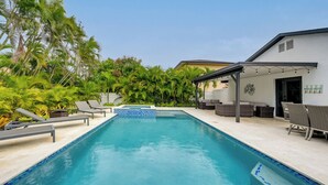 Piscina com espreguiçadeiras e área de estar coberta, rodeada por vegetação exuberante.