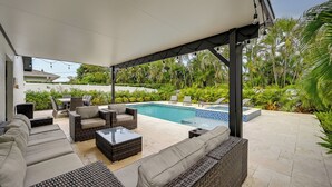 Uma área externa coberta com piscina, mobiliário de vime e vista para vegetação exuberante.