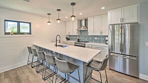 Cozinha moderna com ilha central, banquetas, eletrodomésticos de aço inoxidável e iluminação pendente.