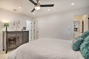 Quarto com cama, penteadeira, ventilador de teto e porta para outro cômodo.