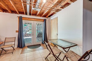 Quarto com mesa de vidro e duas cadeiras, vigas de madeira no teto e porta com vista para o exterior.