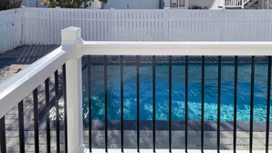Piscina com cerca branca e corrimão preto, rodeada por um deck pavimentado.