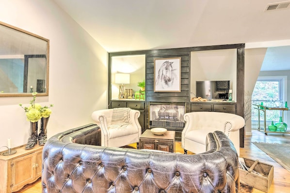 Uma sala de estar com lareira, dois poltronas, um sofá e uma mesa de centro.