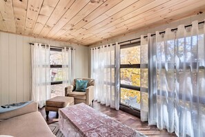 Um quarto aconchegante com teto de madeira, um sofá, uma poltrona e uma mesa.