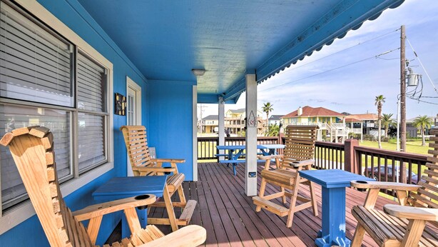Um deck de madeira com área de estar ao ar livre, guarda-corpo azul e vista para edifícios próximos.