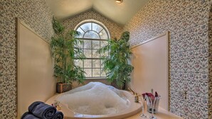 Um quarto de spa com uma banheira grande, duas plantas em vasos e uma janela com vista para árvores.