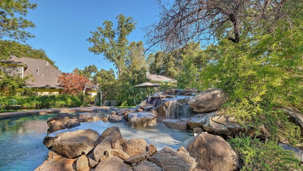 Área de piscina natural com cachoeira, rodeada por pedras e vegetação.