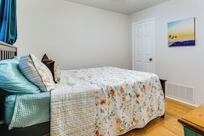 Quarto com cama, mesa de cabeceira, porta e um respiradouro fixado na parede.