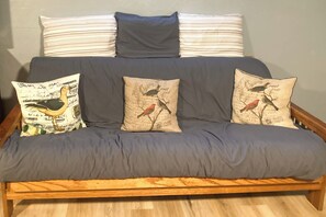 Uma cama com colchão cinza escuro, almofadas listradas e três almofadas decorativas com estampas de pássaros.