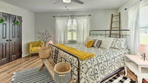 Quarto com cama, escrivaninha, cadeira, ventoinha no teto e janela com cortinas.