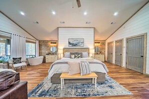 Um quarto espaçoso com uma cama grande, um espaço de estar com um banco, uma banheira e vista para o exterior.